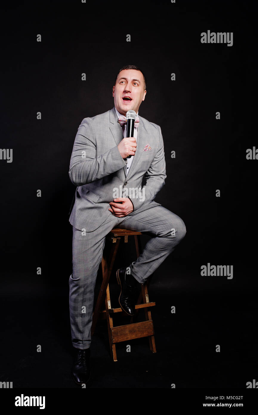 Handsome man in gray suit with microphone against black background on ...