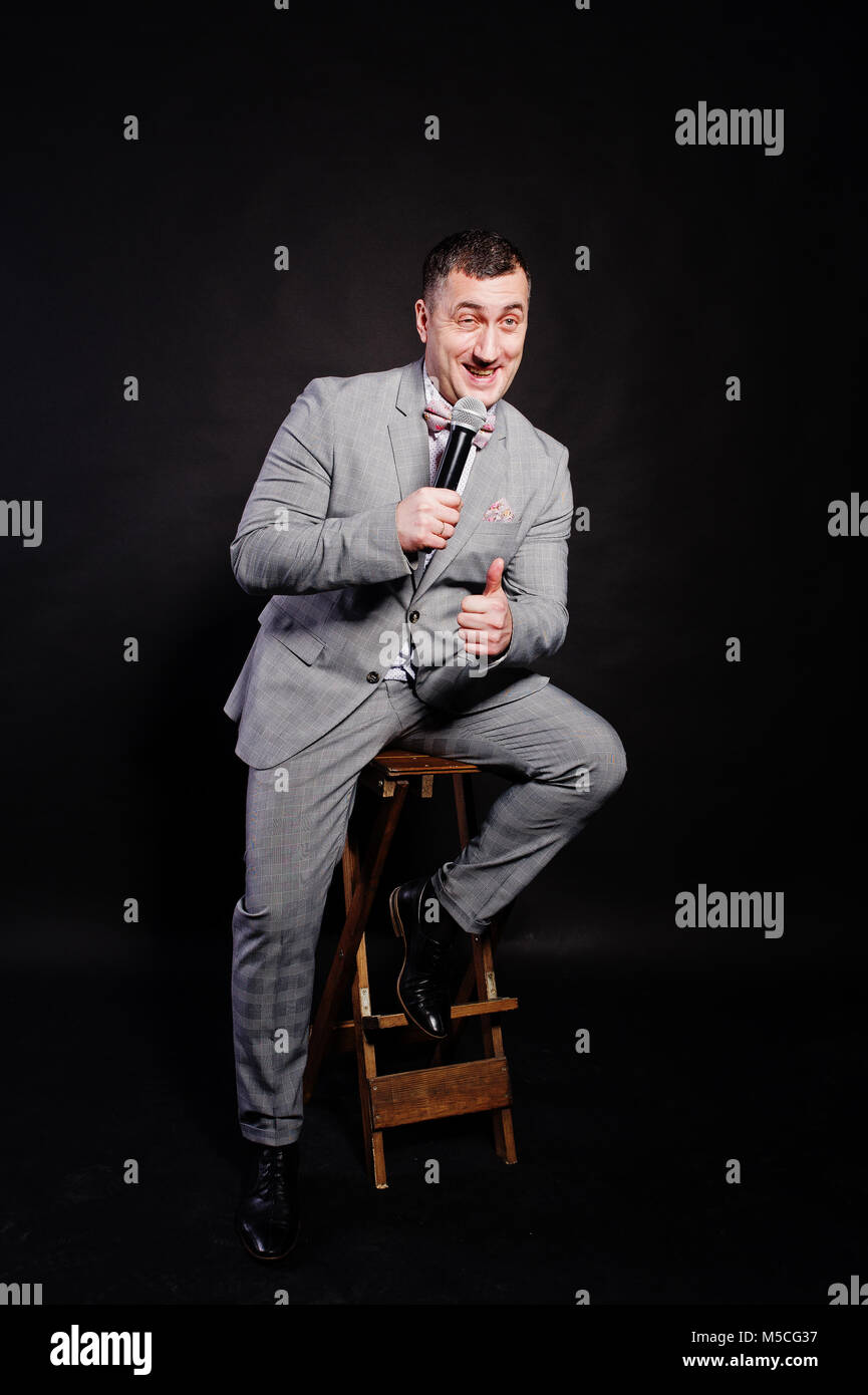 Handsome man in gray suit with microphone against black background on ...