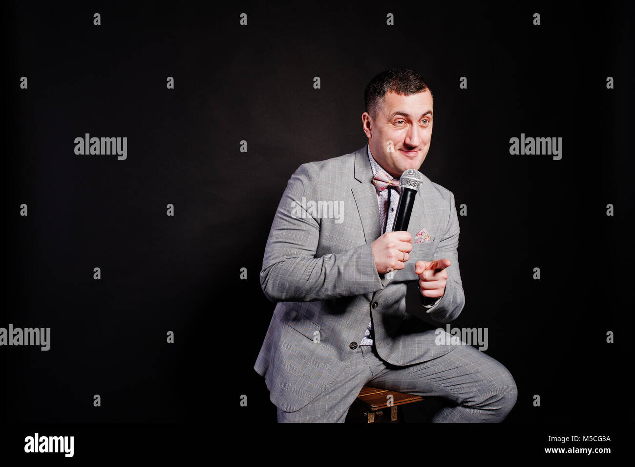 Handsome man in gray suit with microphone against black background on ...
