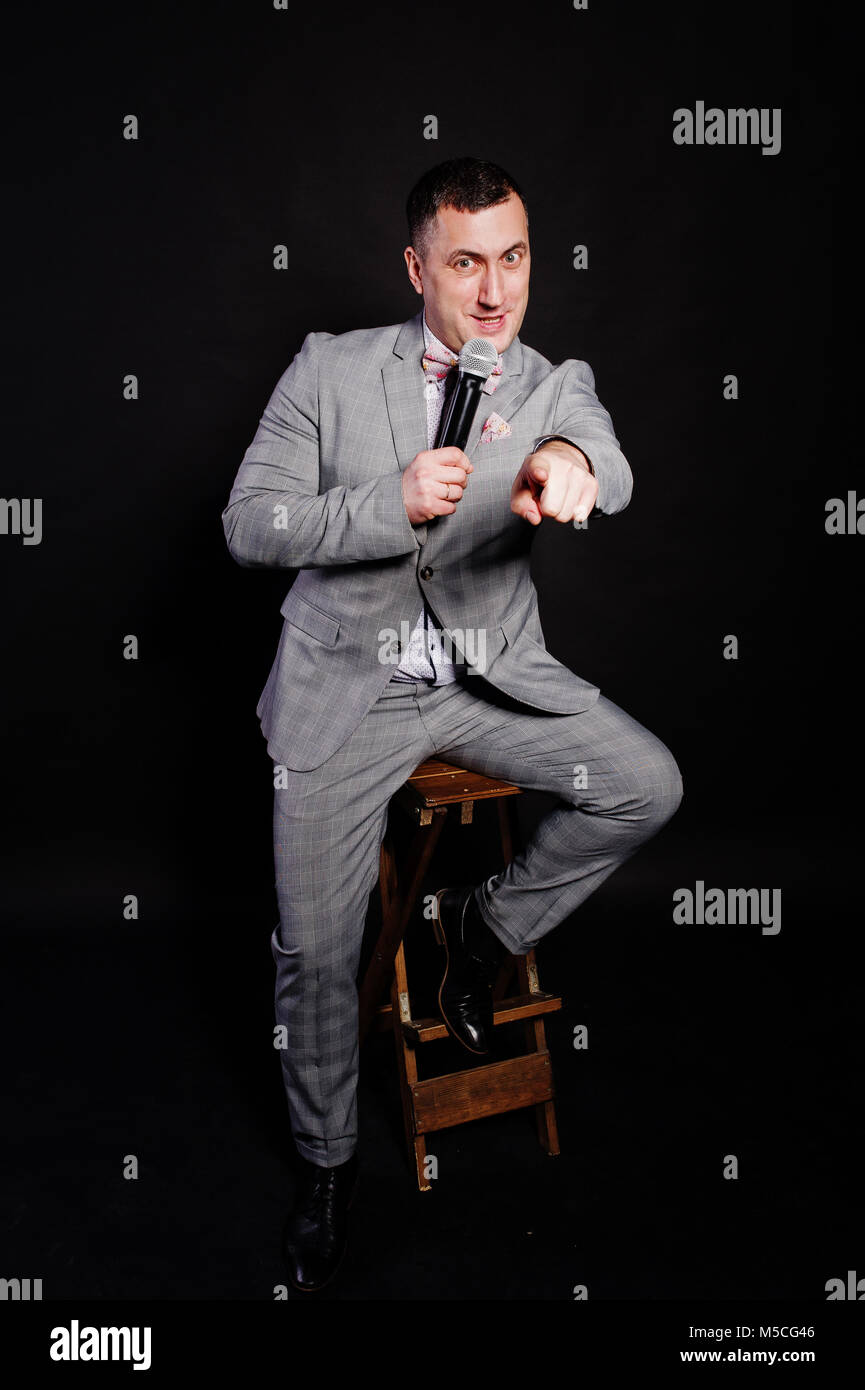 Handsome man in gray suit with microphone against black background on ...