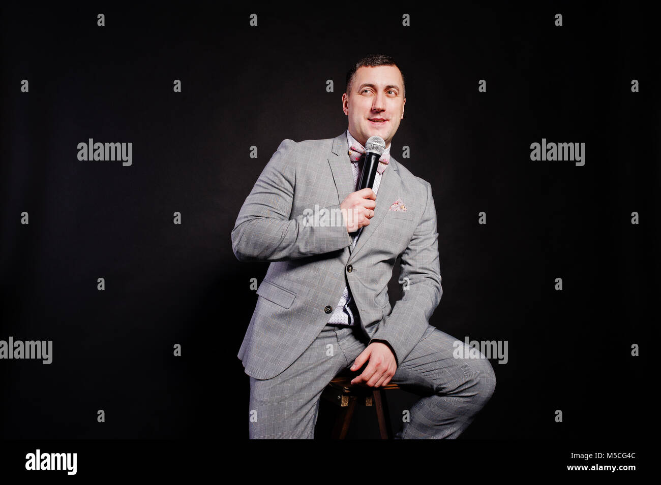 Handsome man in gray suit with microphone against black background on ...