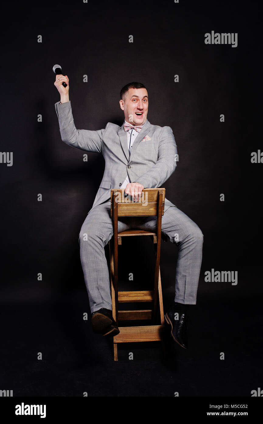 Handsome man in gray suit with microphone against black background on ...