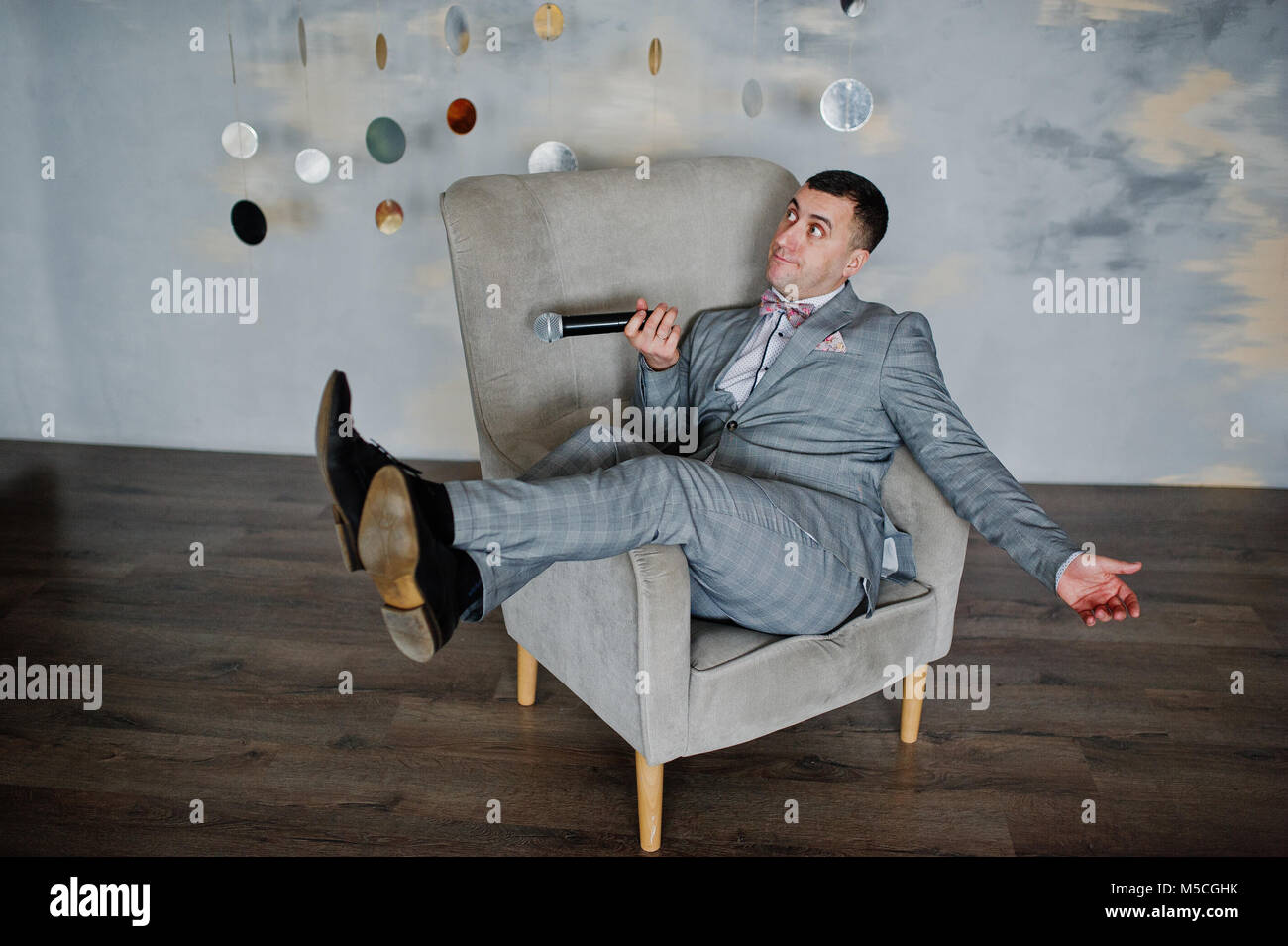 Handsome man in gray suit with microphone sitting on chair background ...