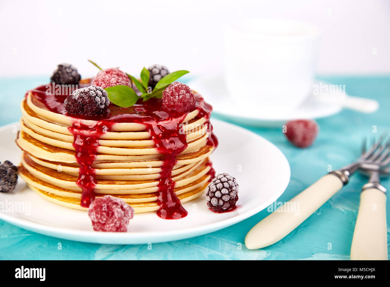 American pancake with jam and frozen raspberry with tea on blue ...