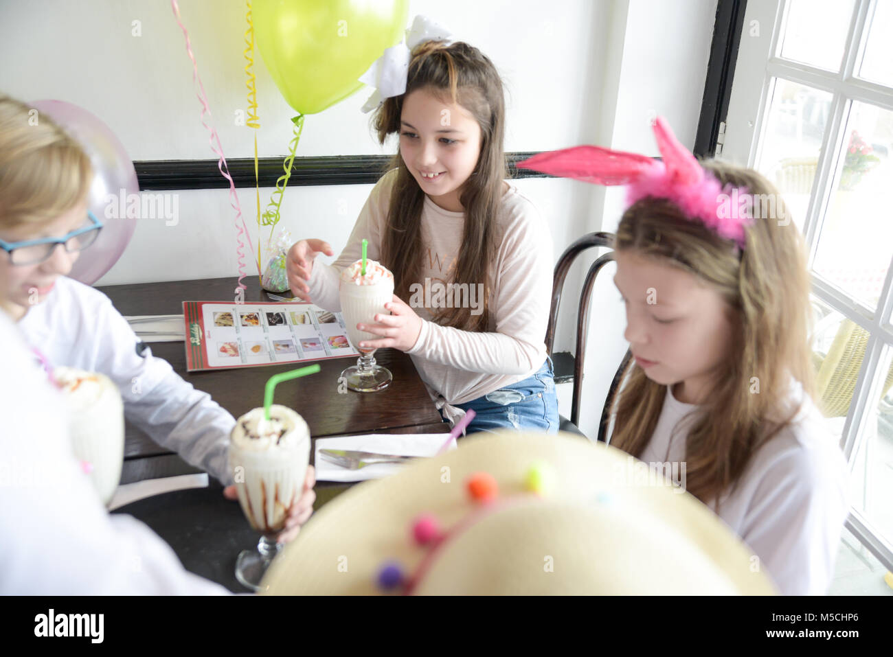 Three young children are sitting at a party table eating fried food and ...