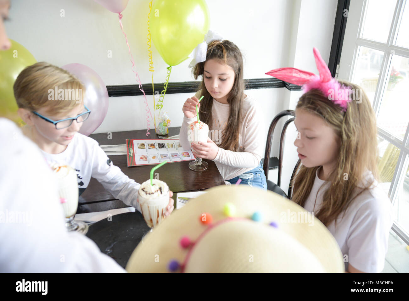 Three young children are sitting at a party table eating fried food and ...