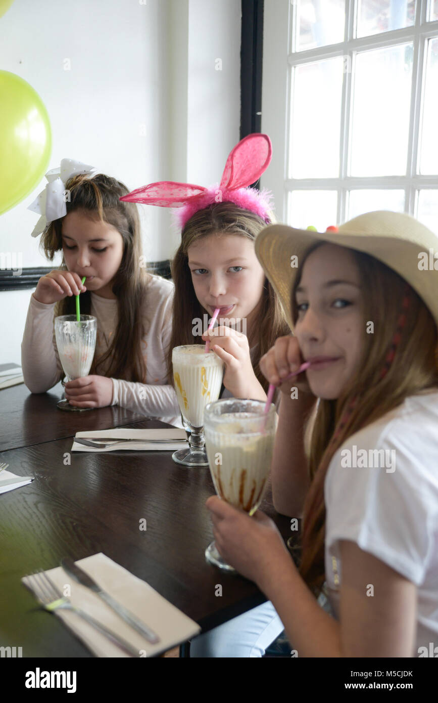 Three young children are sitting at a party table eating fried food and ...