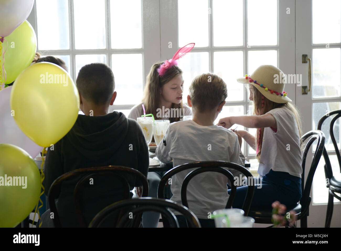 Four young children are sitting at a party table eating fried food and ...