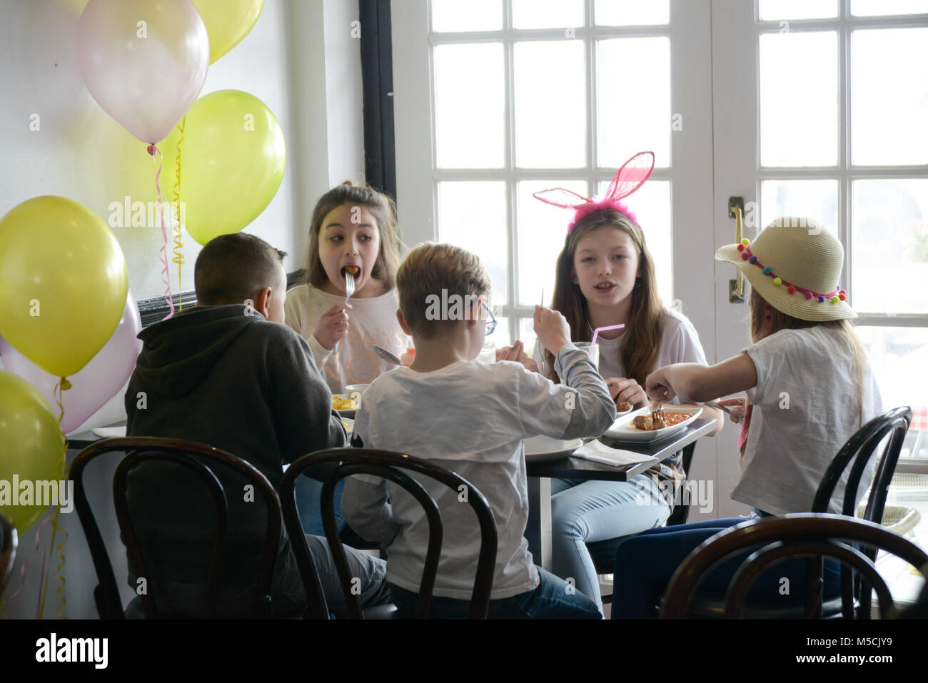 Five young children are sitting at a party table eating fried food and ...