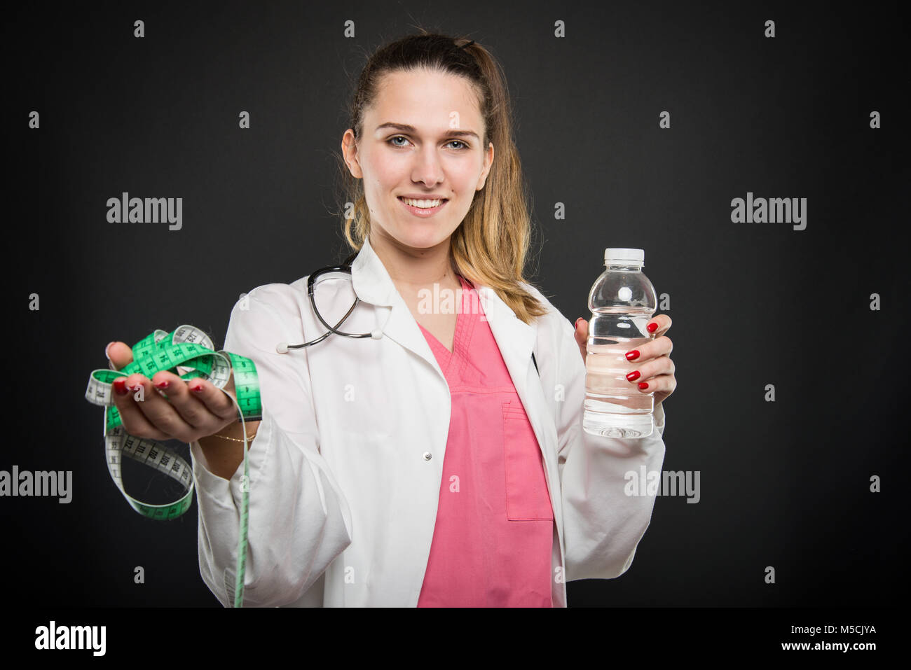 Female doctor portrait holding measuring tape and bottle of water on ...