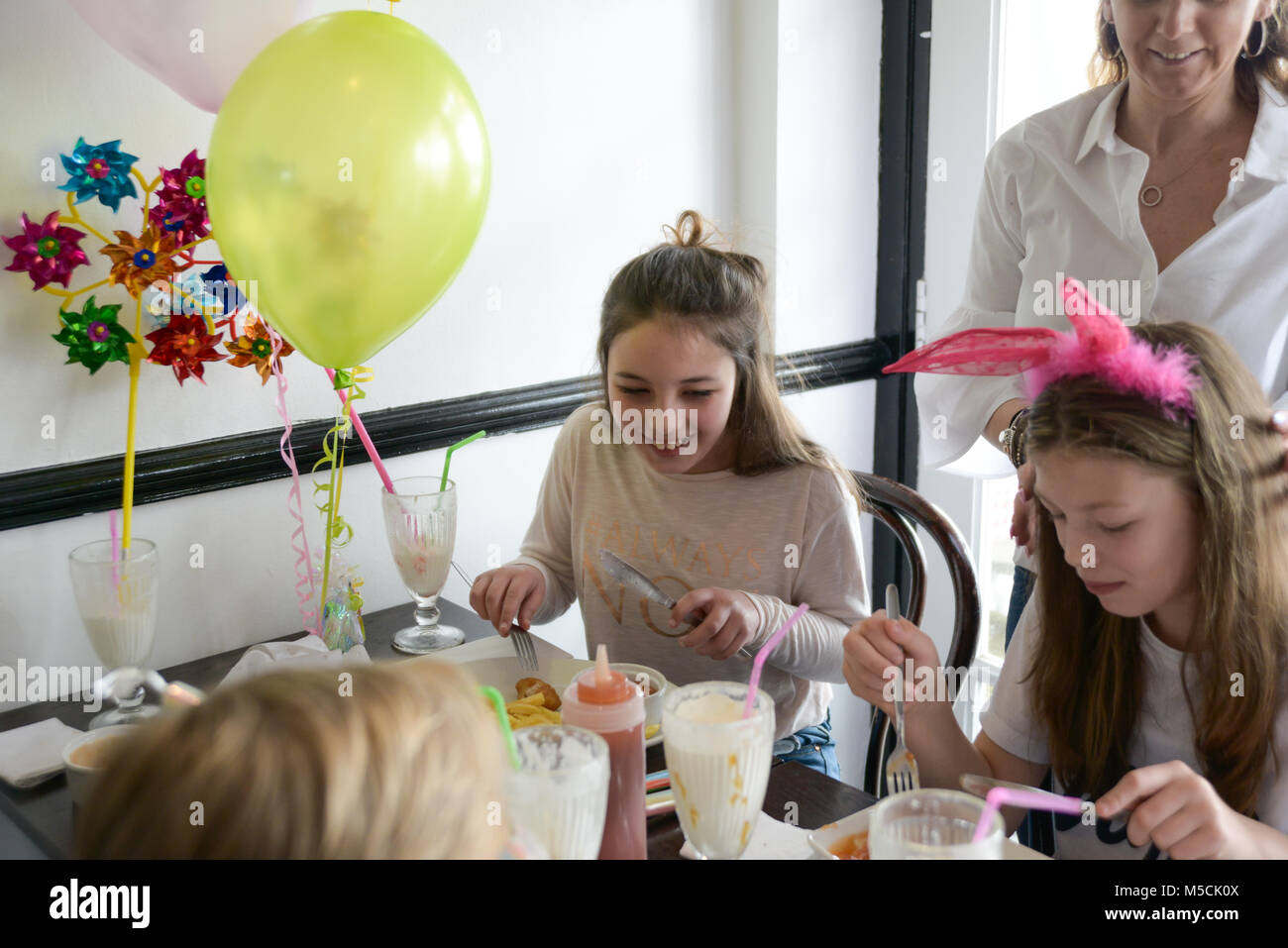Four young children are sitting at a party table eating fried food and ...