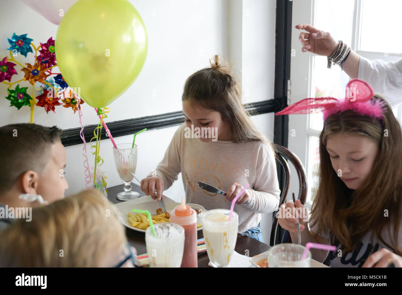 Four young children are sitting at a party table eating fried food and ...