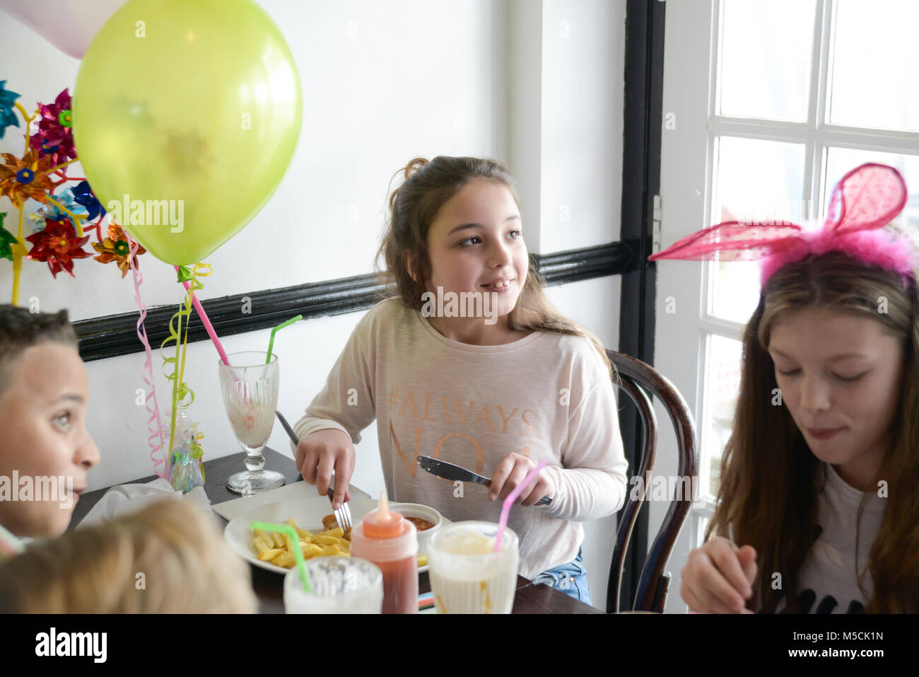 Four young children are sitting at a party table eating fried food and ...