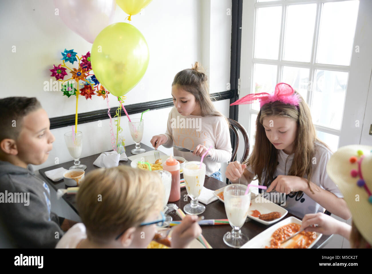 Five young children are sitting at a party table eating fried food and ...