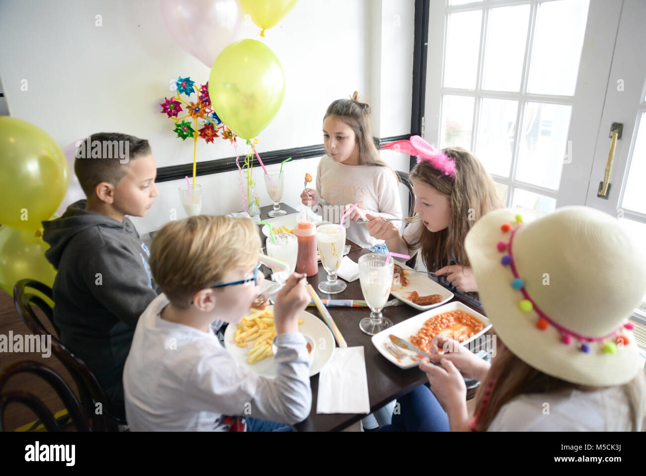 Five young children are sitting at a party table eating fried food and ...