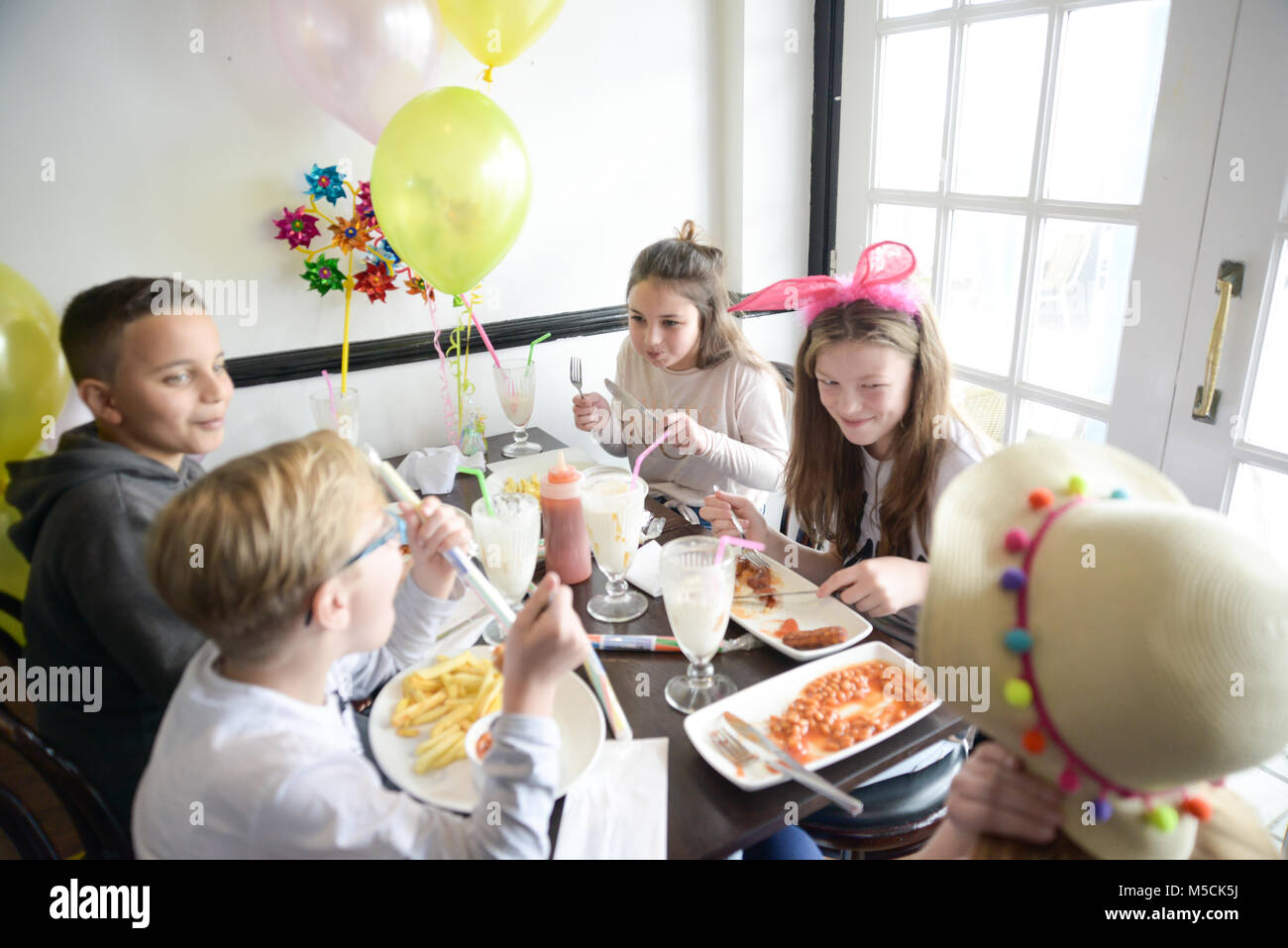 Five young children are sitting at a party table eating fried food and ...