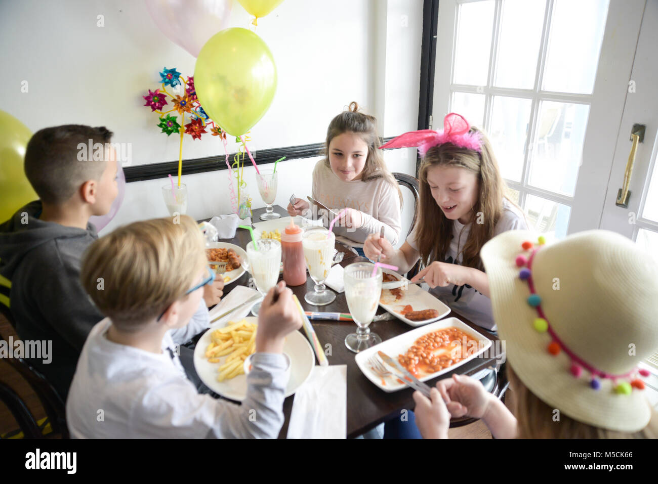 Five young children are sitting at a party table eating fried food and ...