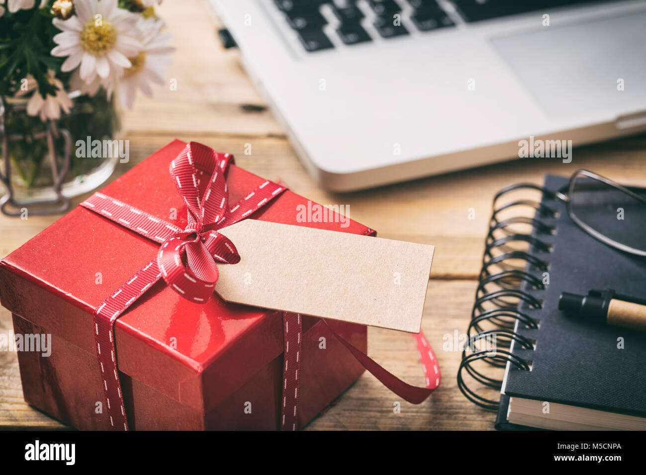 Red gift box with red ribbon and empty blank tag, blur office desk ...