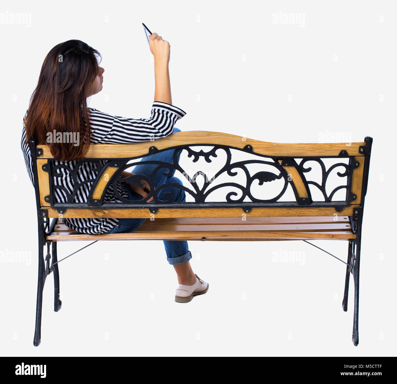 back view of woman sitting on bench and looks at the screen of the ...