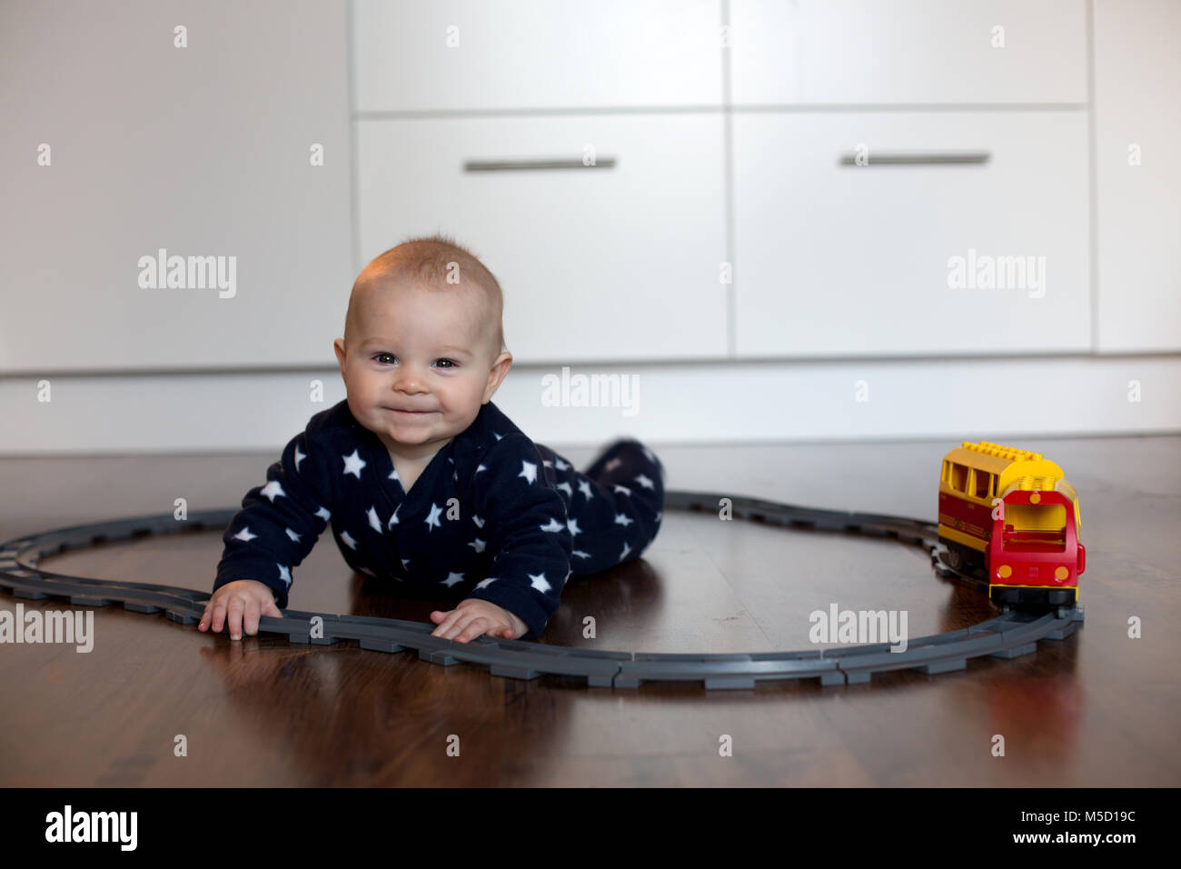 Little baby boy, playing with train and railroad at home in living room ...