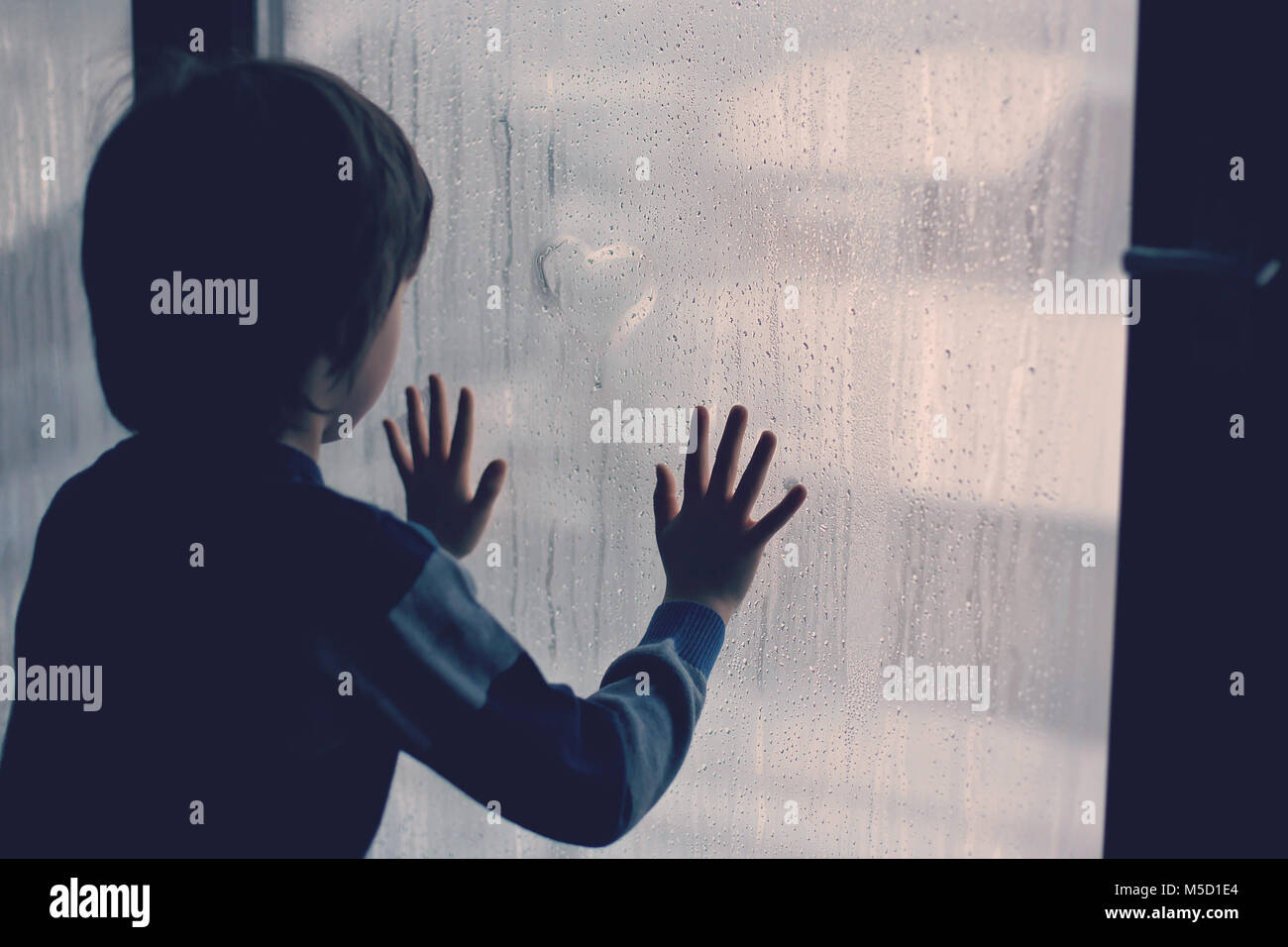 Little boy, leaving finger prints and drawing hearts on a window at ...