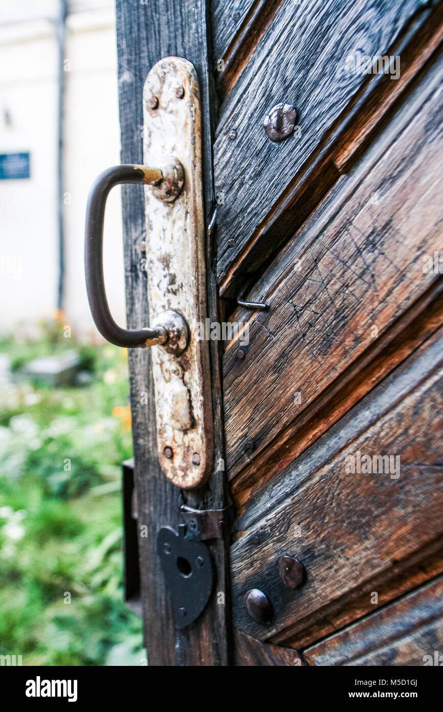 closeup part of age-old wooden door slightly open into yard with rusty ...