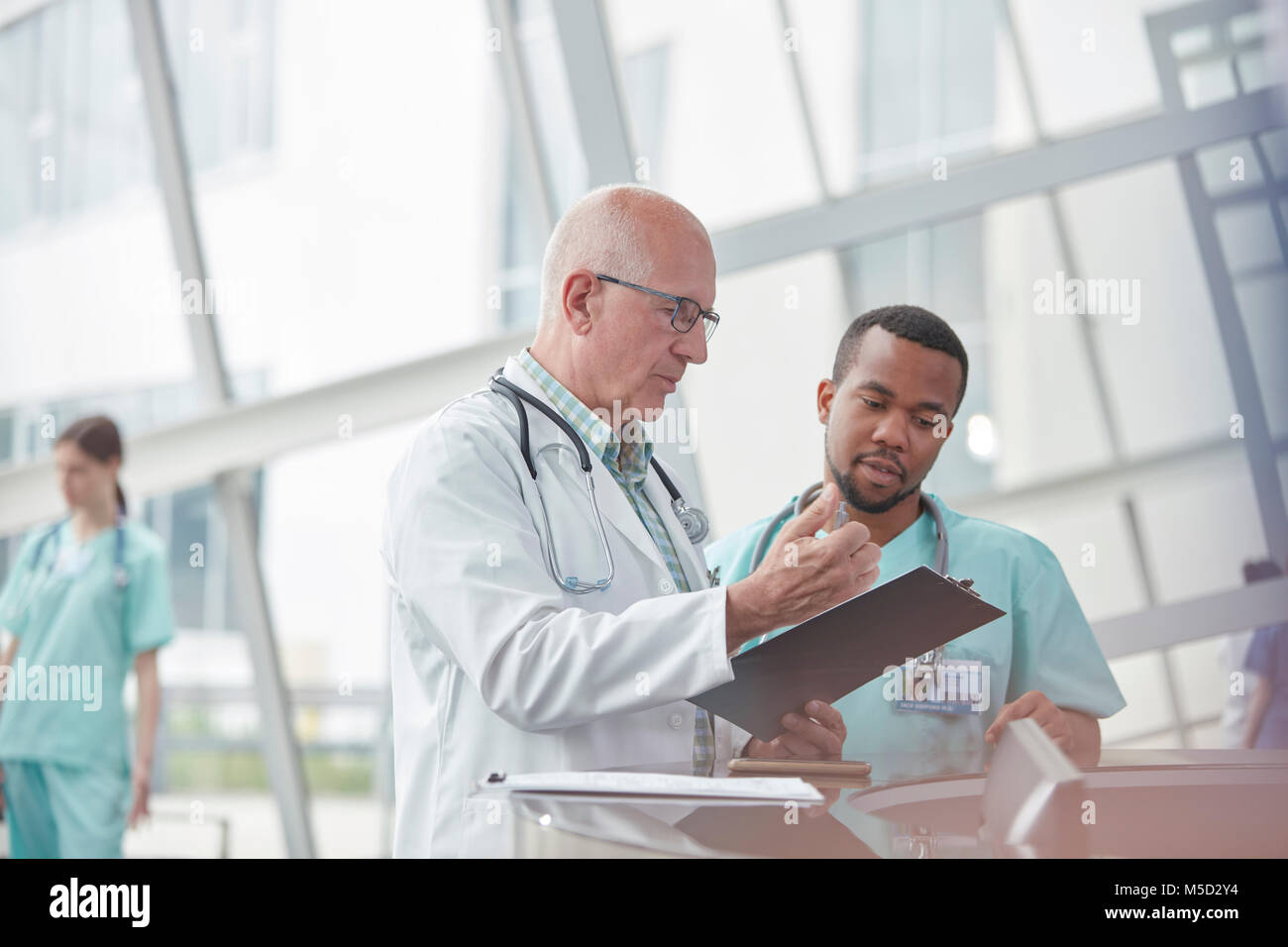 Male doctor and nurse with clipboard talking in hospital lobby Stock ...