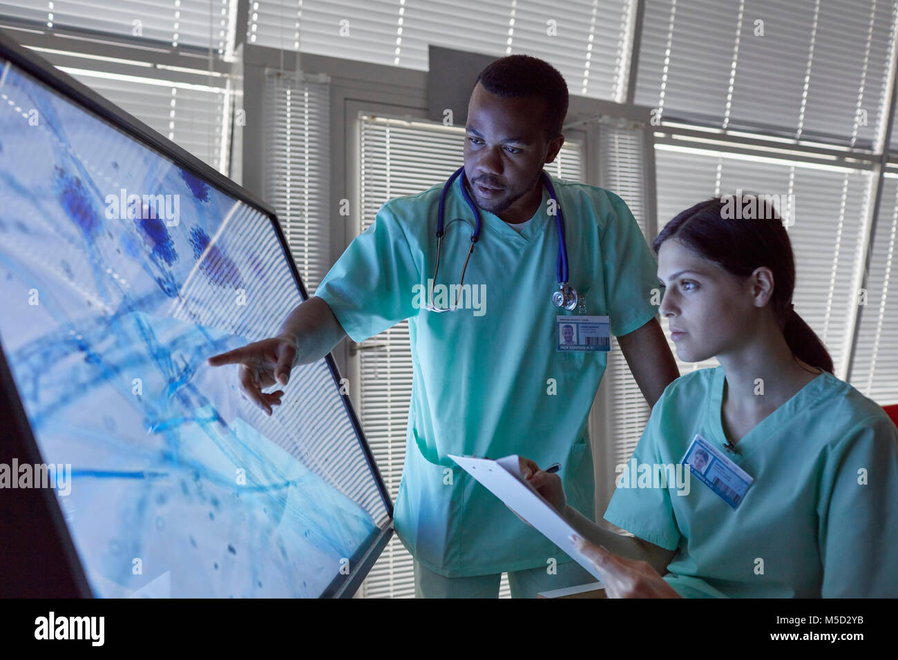 Nurses with clipboard examining magnified microscope slide on computer ...
