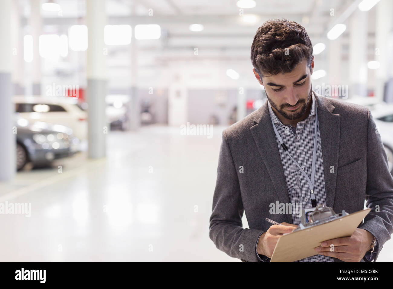Car salesman writing on clipboard in car dealership auto repair shop ...