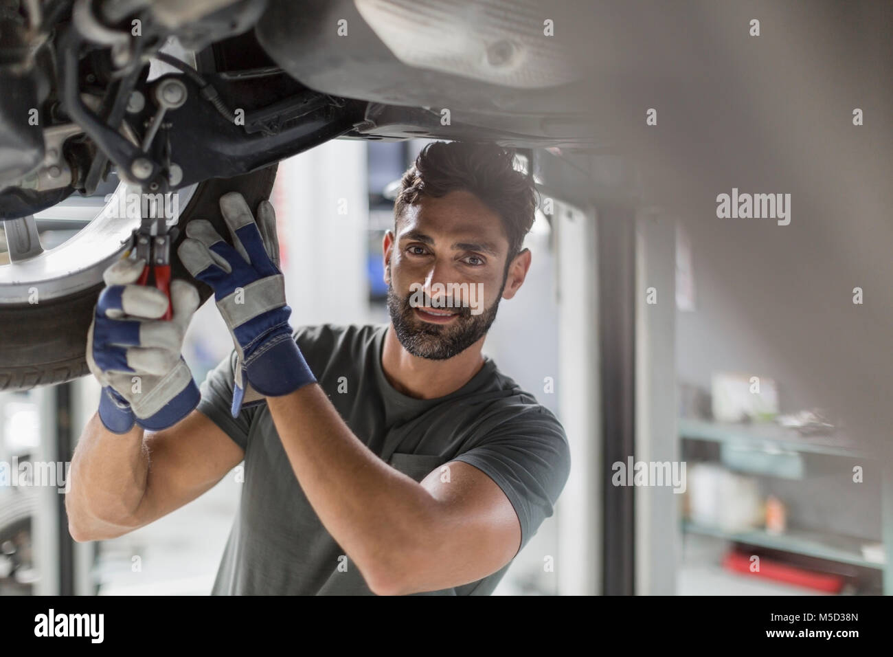 Portrait confident male auto mechanic working under car in auto repair ...
