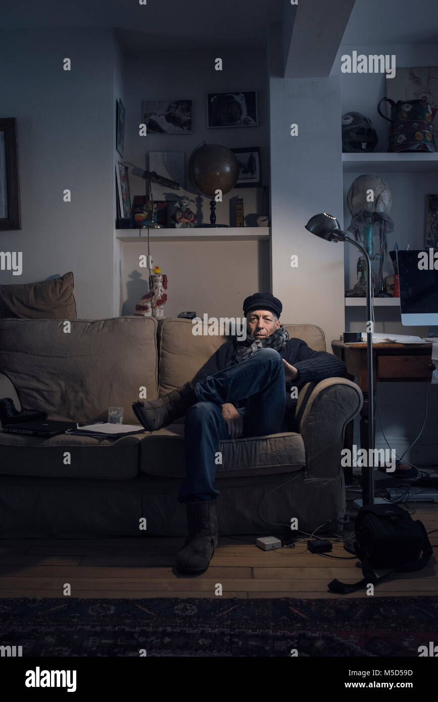 an elder man sits relaxed on the sofa wrapped up warm in a scarf, hat ...