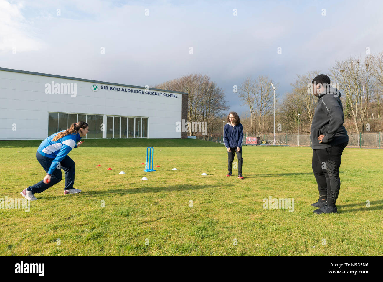 students practice playing cricket on a school playing field as part of ...