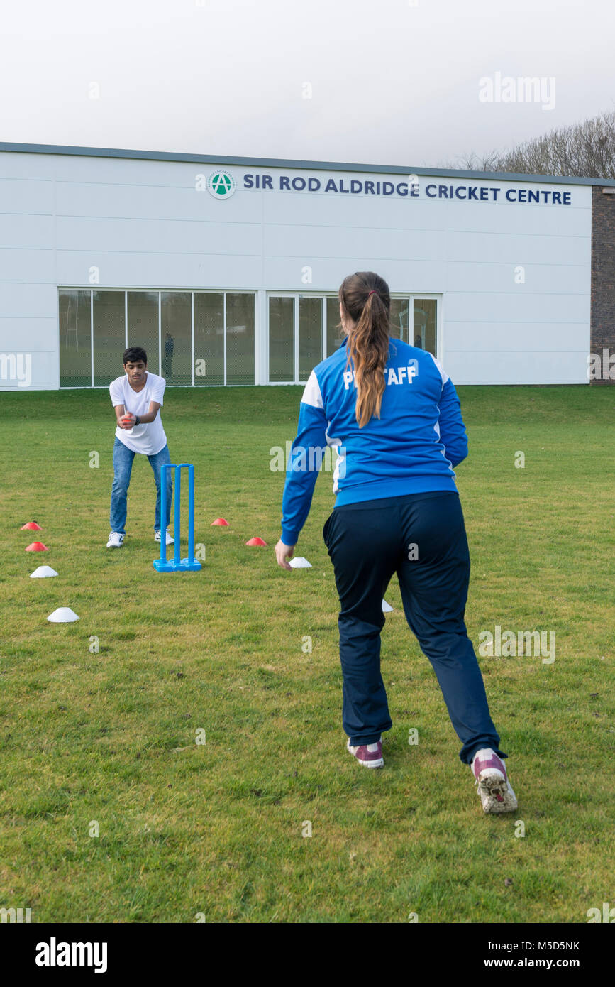 students practice playing cricket on a school playing field as part of ...