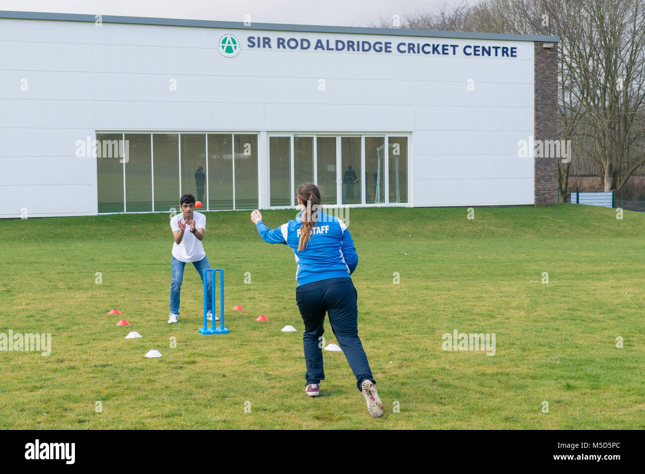 students practice playing cricket on a school playing field as part of ...