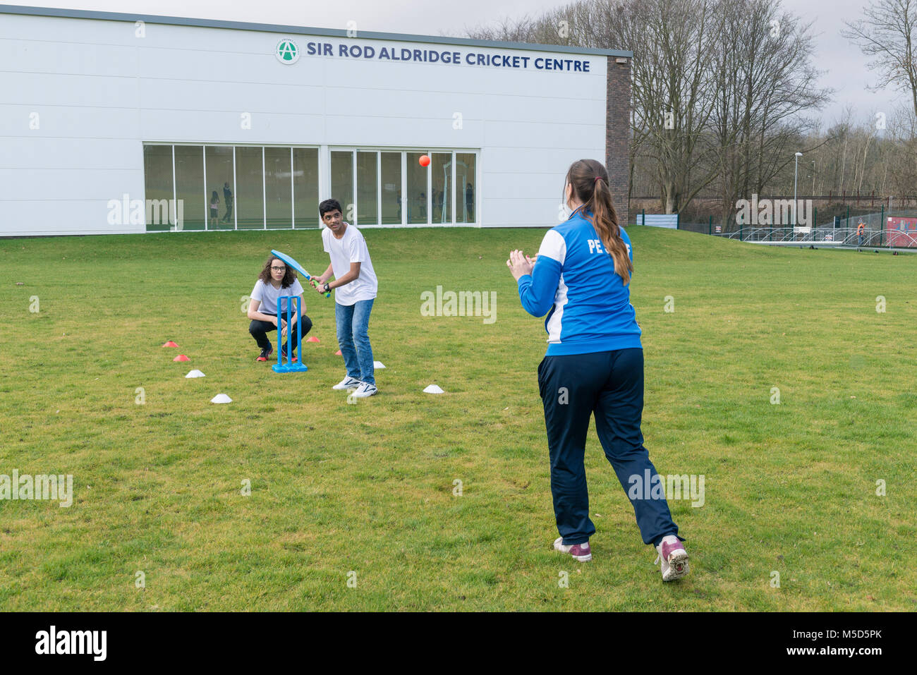 students practice playing cricket on a school playing field as part of ...
