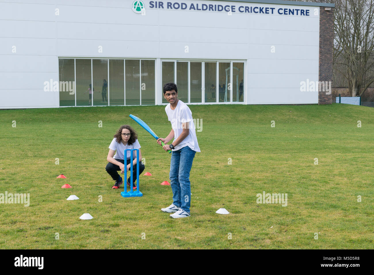 students practice playing cricket on a school playing field as part of ...