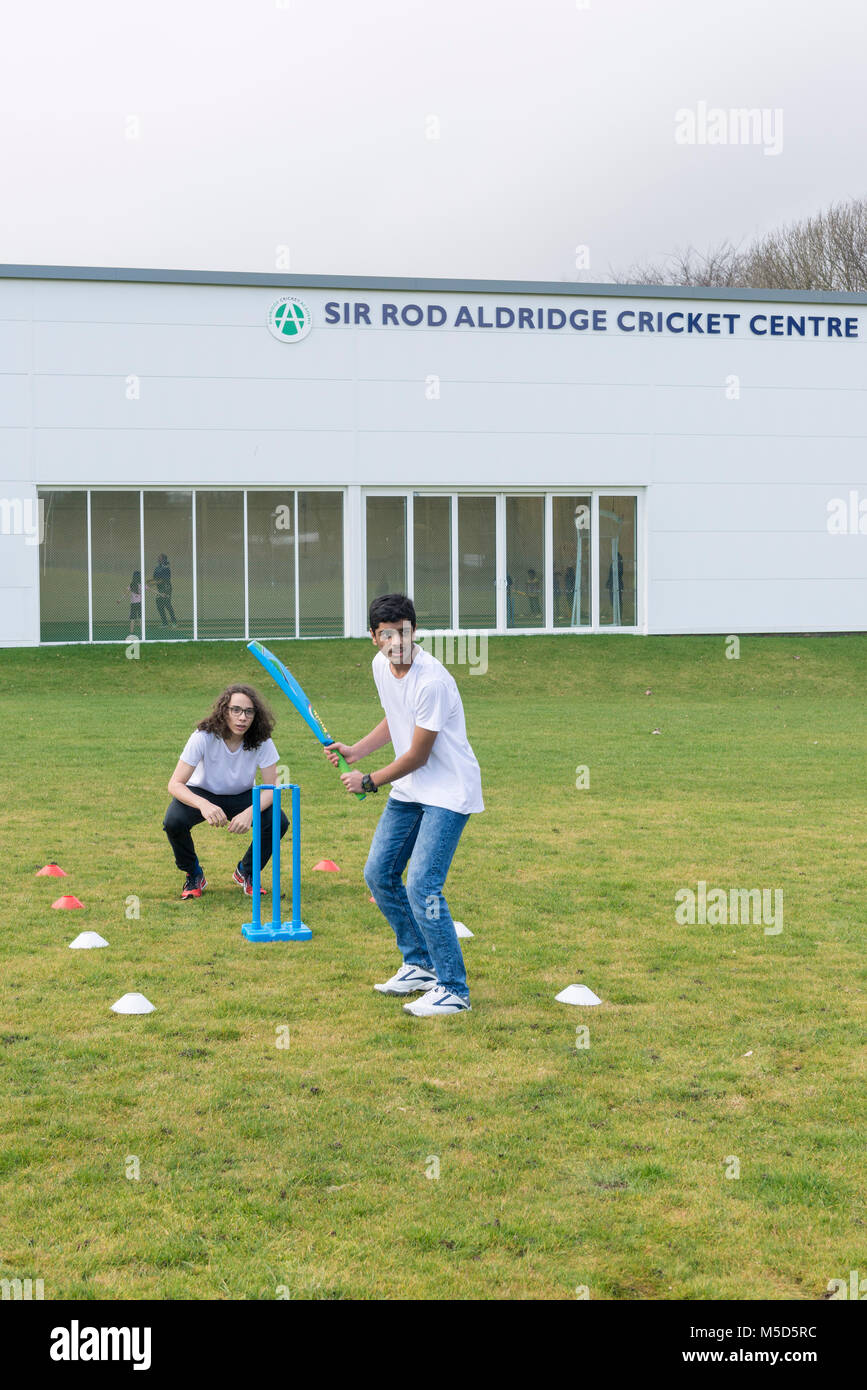 students practice playing cricket on a school playing field as part of ...