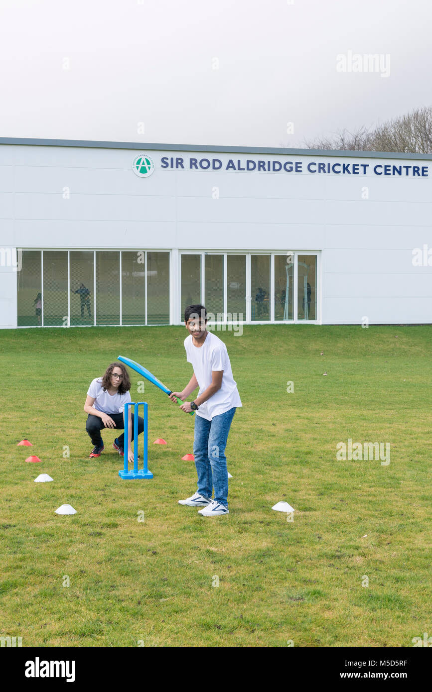 students practice playing cricket on a school playing field as part of ...