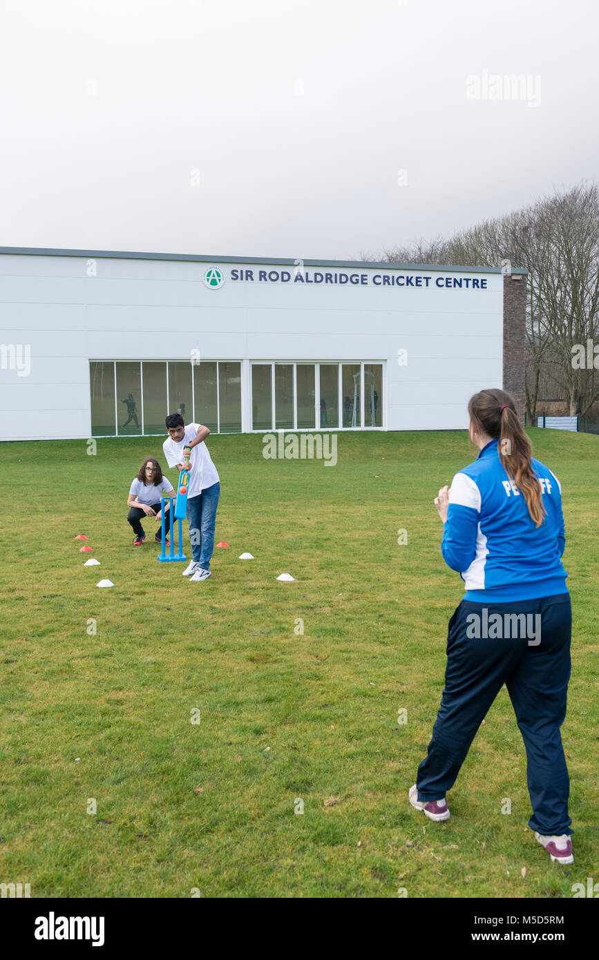 students practice playing cricket on a school playing field as part of ...