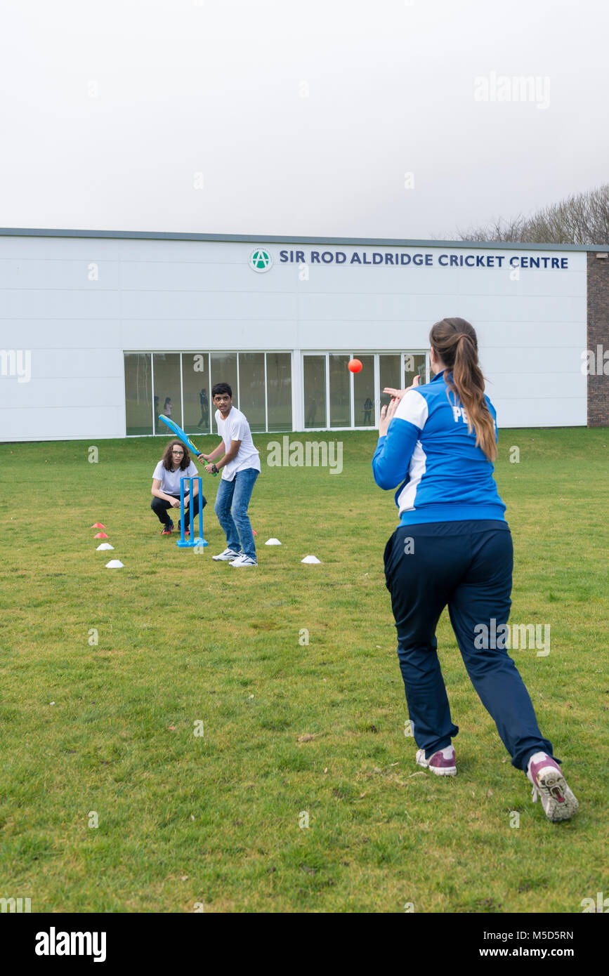 students practice playing cricket on a school playing field as part of ...