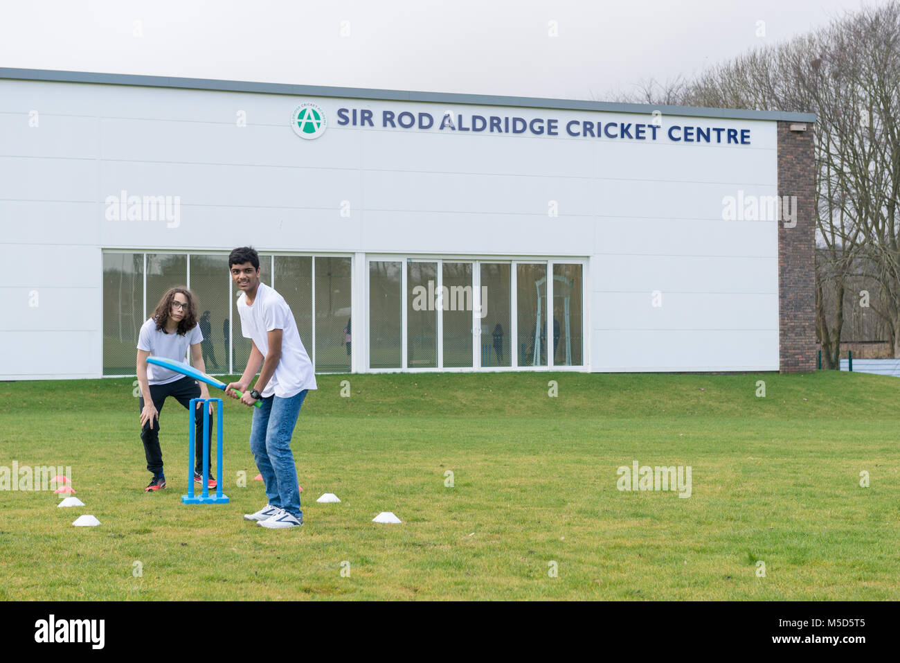 students practice playing cricket on a school playing field as part of ...