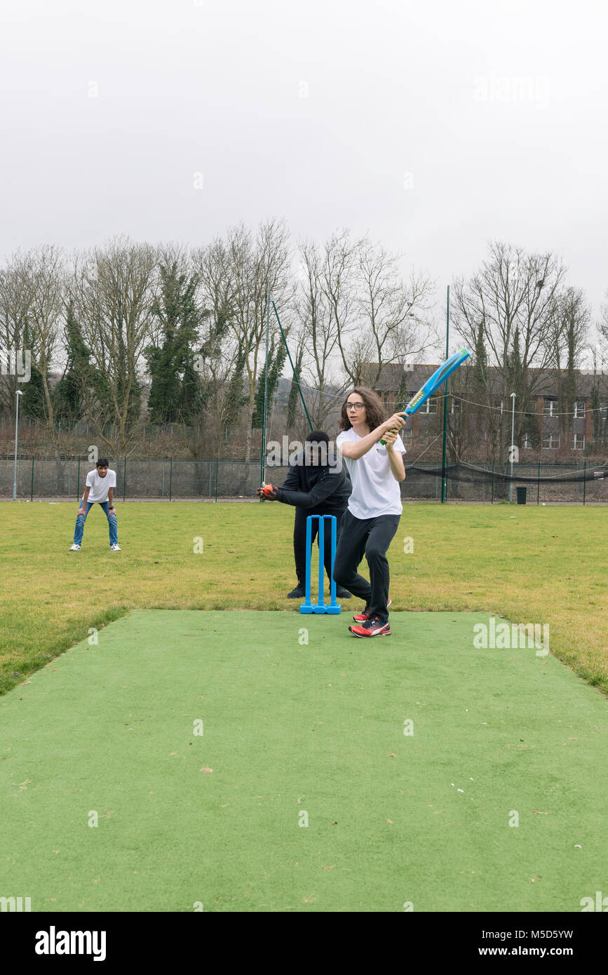 students practice playing cricket on a school playing field as part of ...