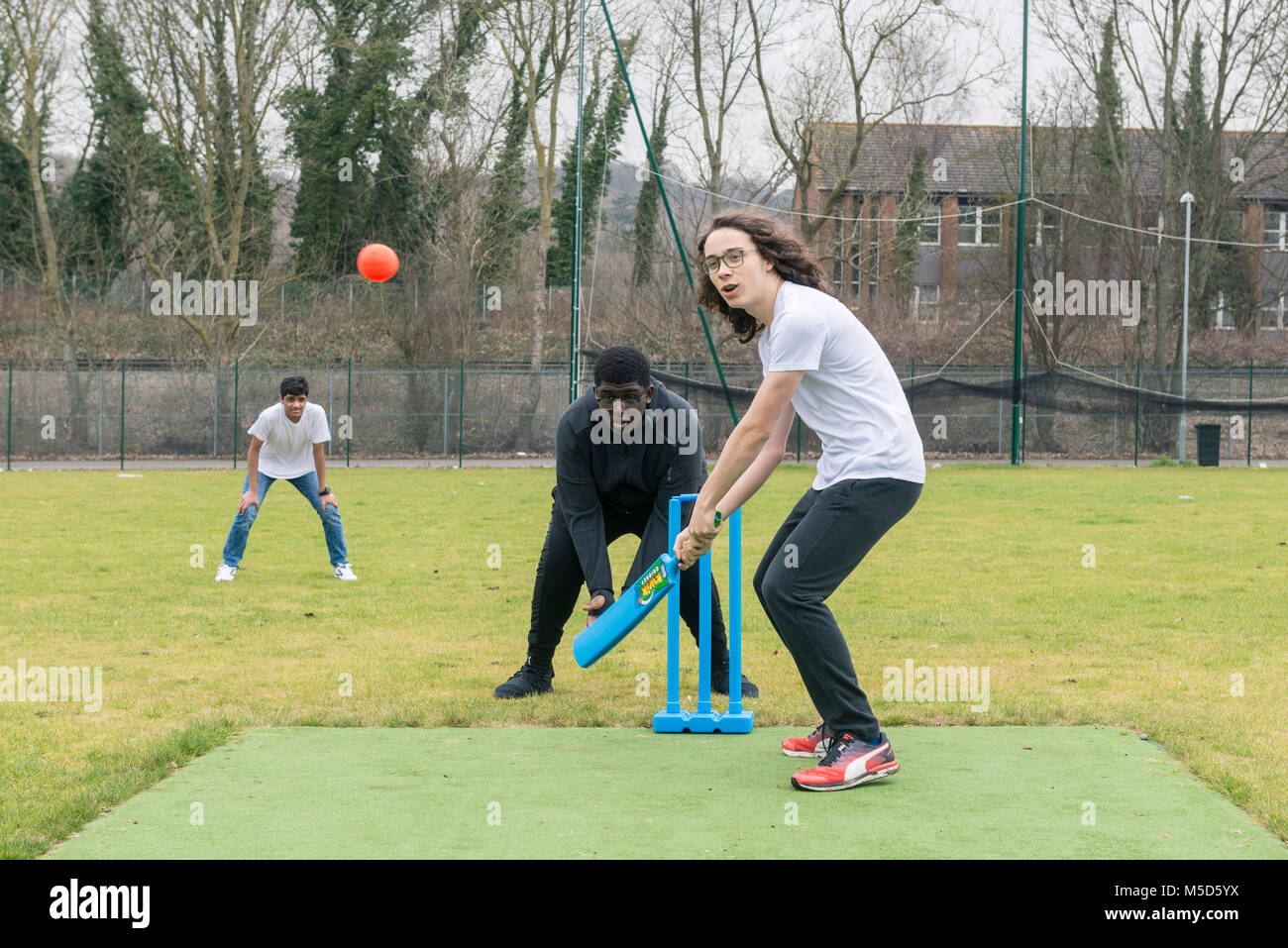 students practice playing cricket on a school playing field as part of ...