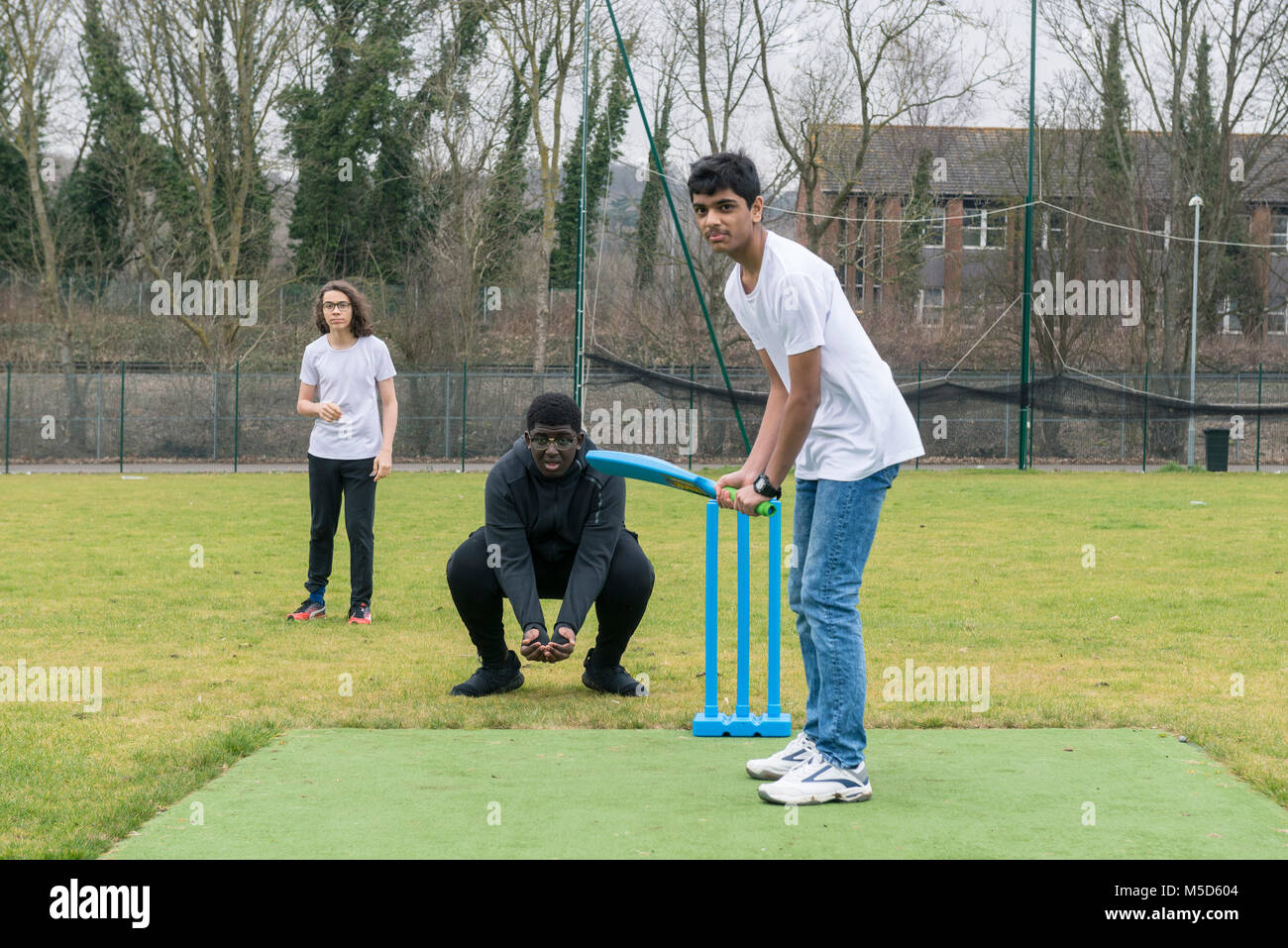 students practice playing cricket on a school playing field as part of ...