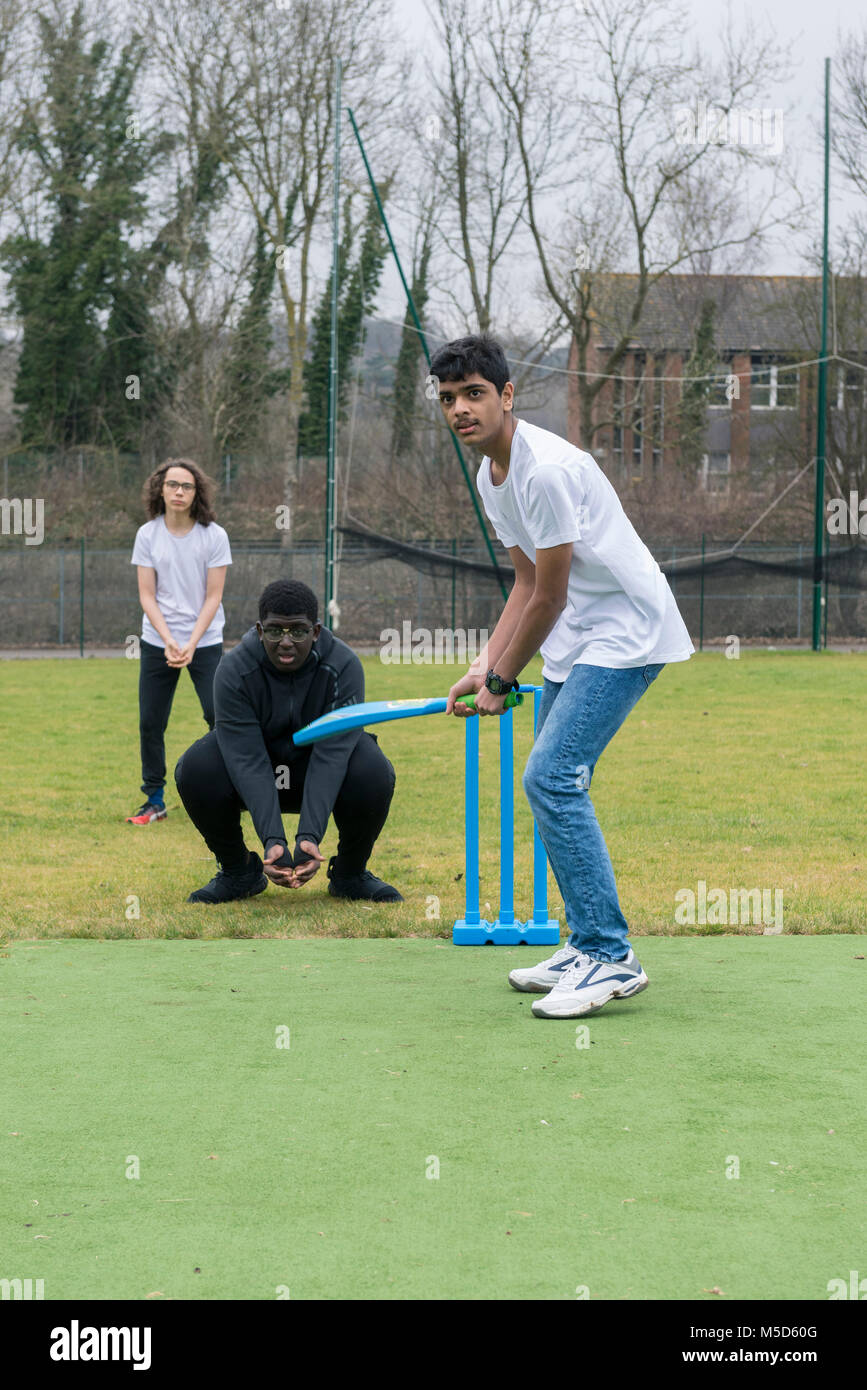 students practice playing cricket on a school playing field as part of ...