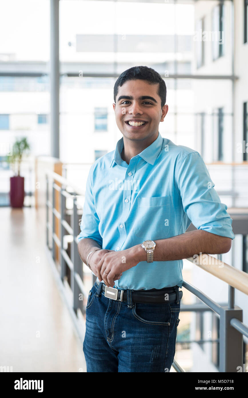 a confident, young man standing in an office building in a blue shirt ...