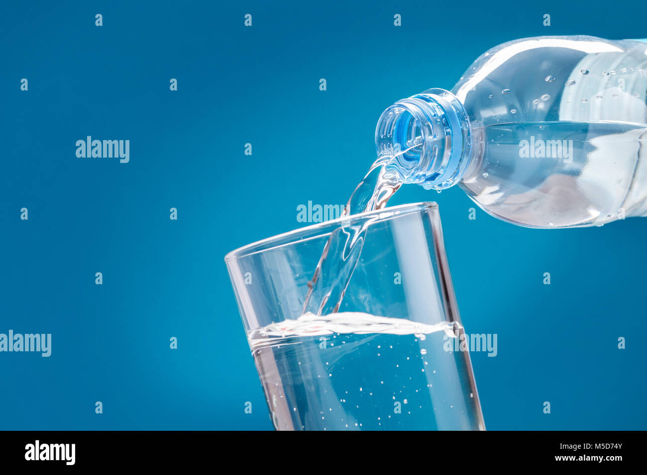 Pouring Refreshing Water From A Plastic Bottle Into A Glass On A Blue Background Stock Photo - Alamy