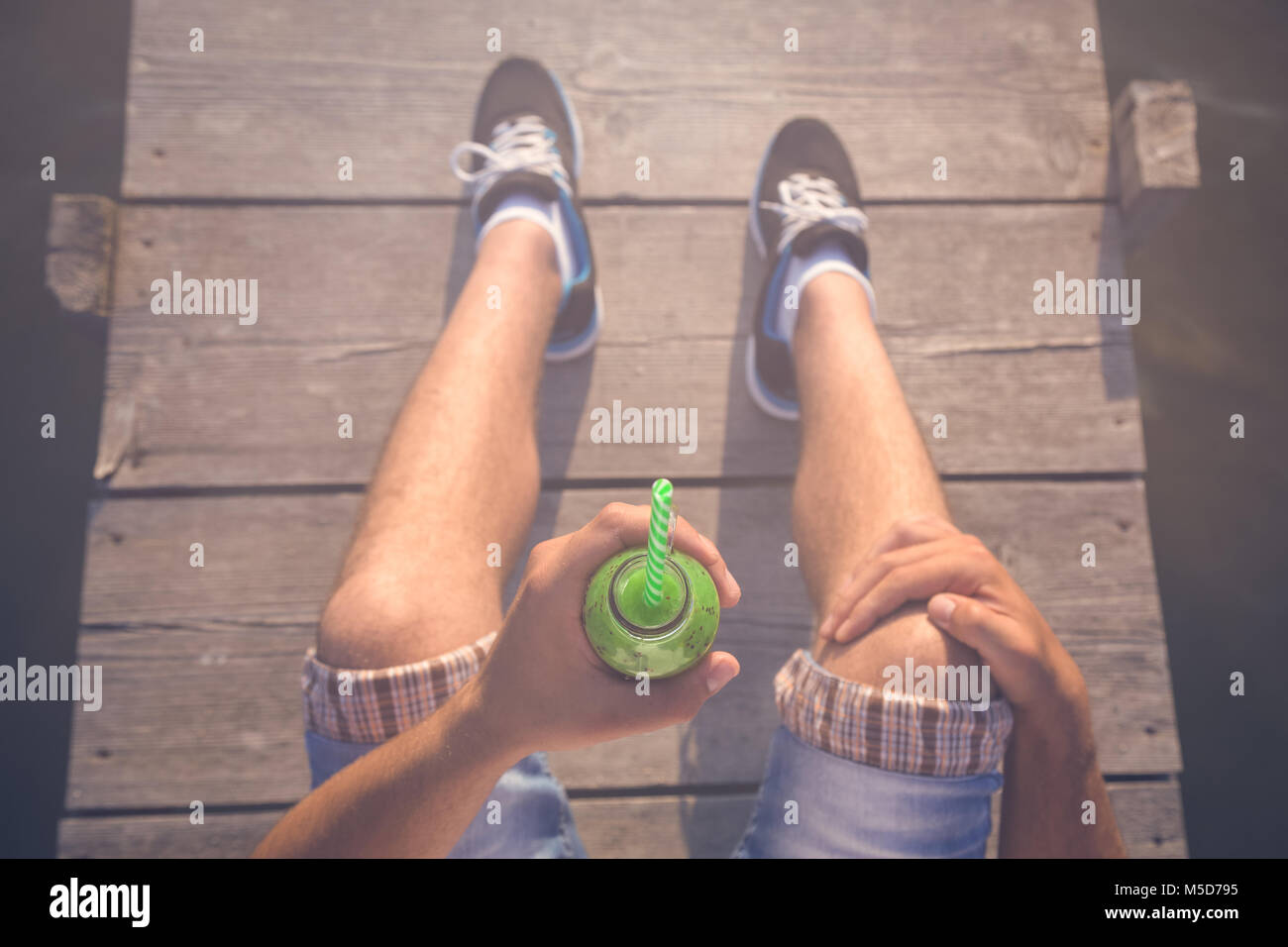 Top down viewpoint of man sitting on pier and holding glass of fresh ...