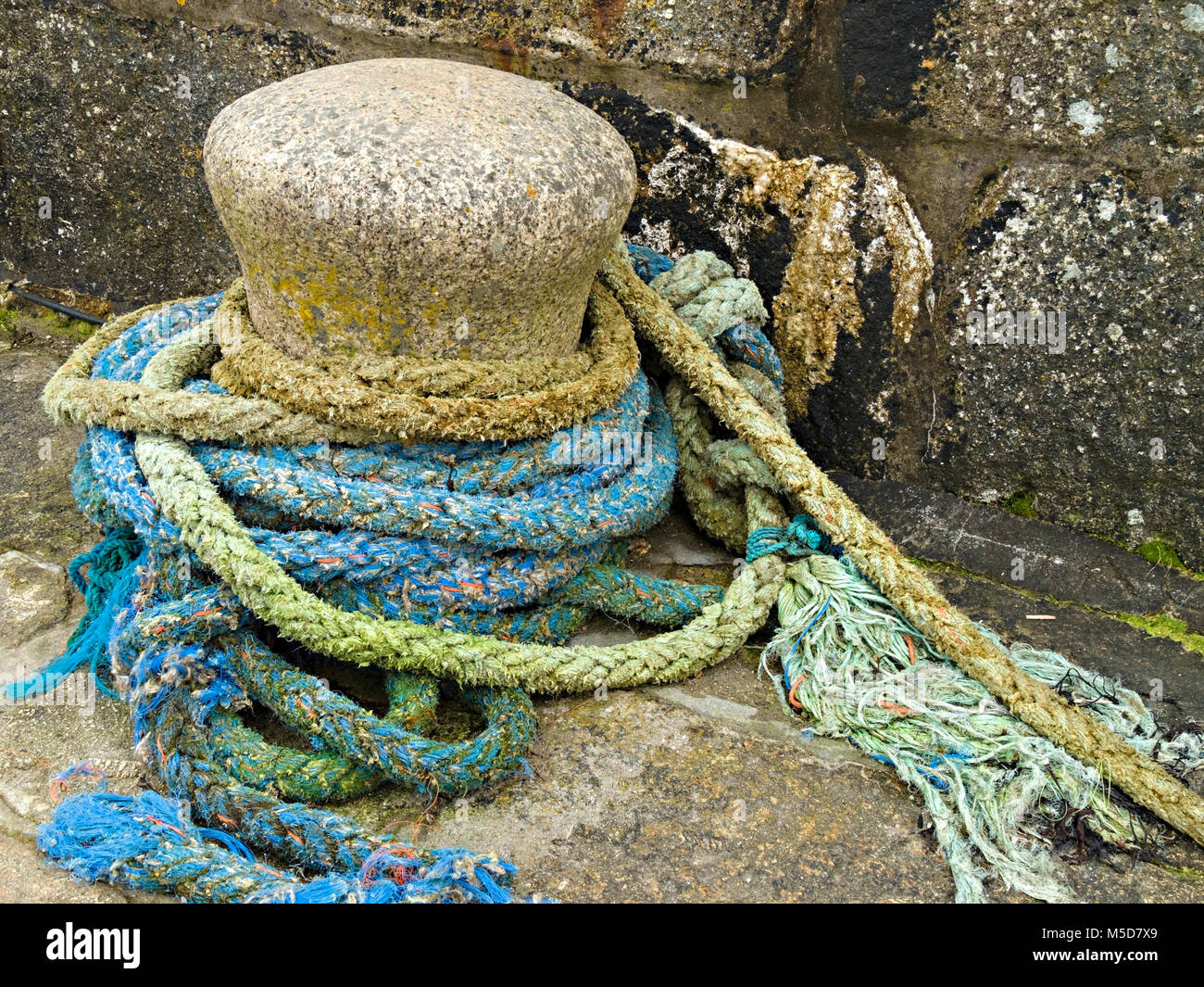 Stone harbour wall and granite mooring bollard with ropes around it ...