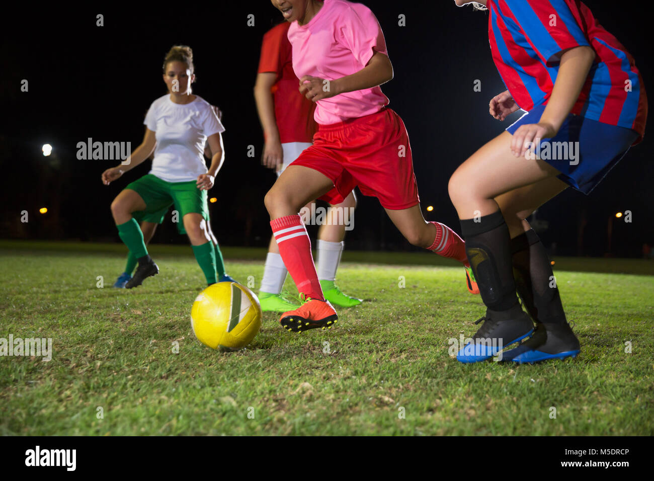 Young female soccer players playing on field at night, running for ball ...